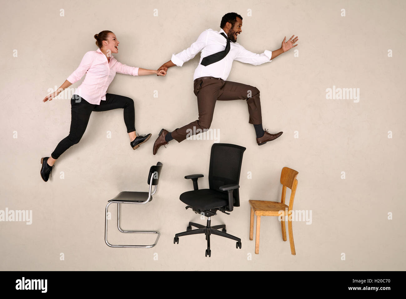 Businessman jumping with his female colleague over chairs Stock Photo ...