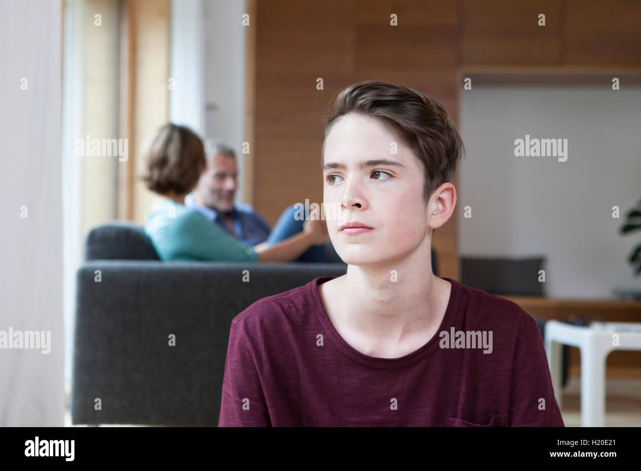 Thoughtful teenage boy at home with parents in background Stock Photo ...