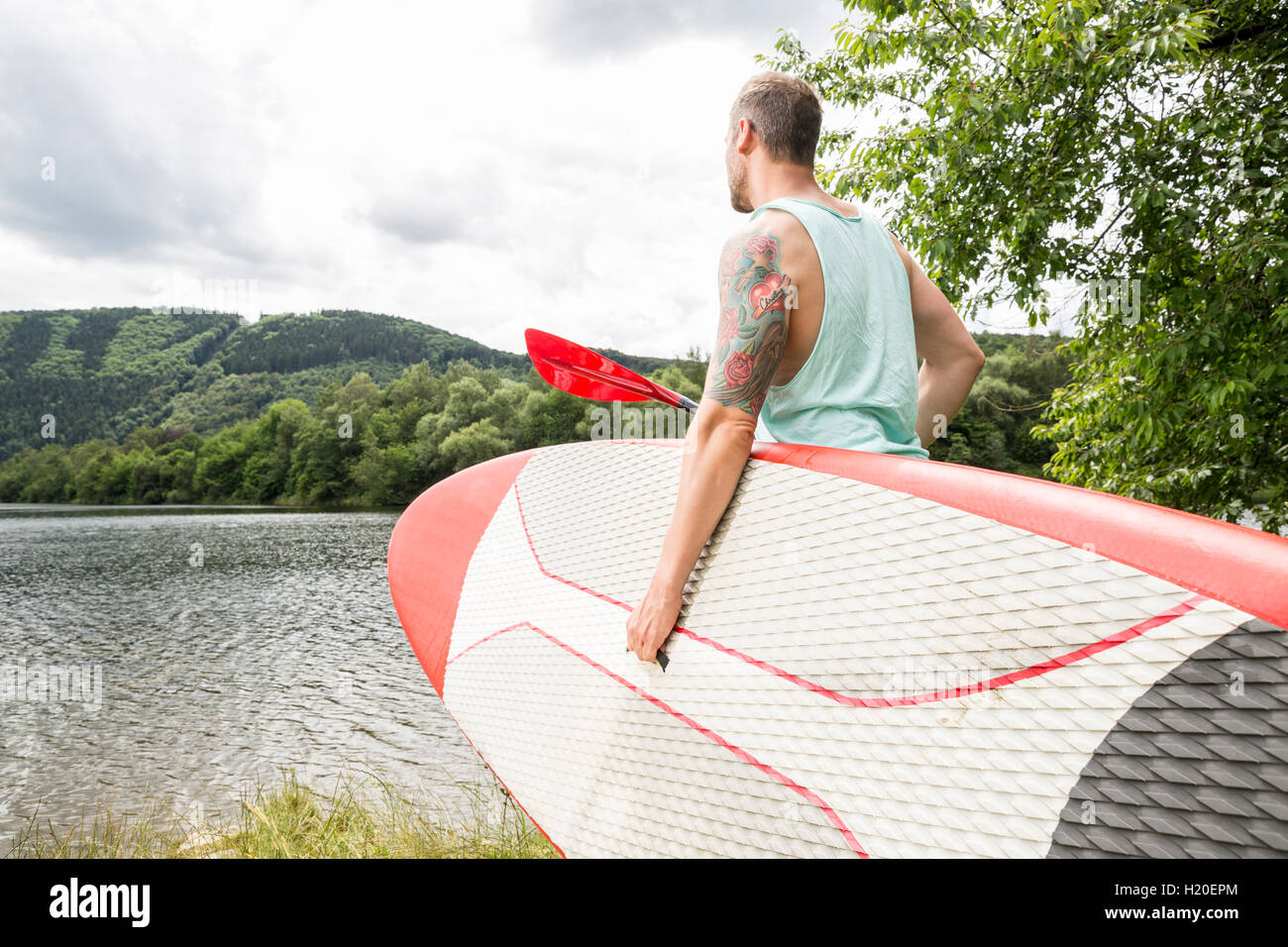 Man carrying stand up paddle board at lakeside Stock Photo - Alamy