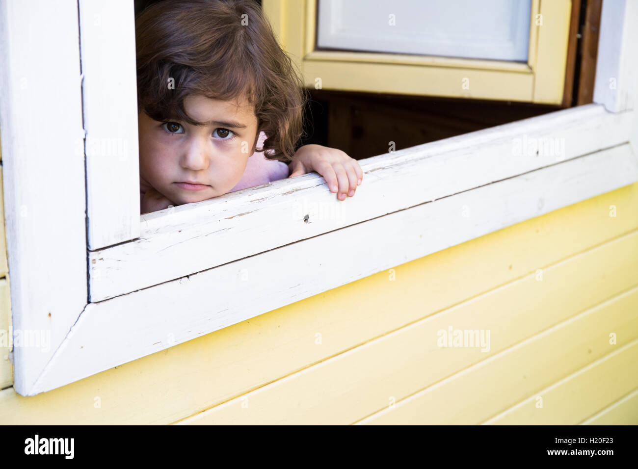 Portrait of little girl looking through open window Stock Photo - Alamy