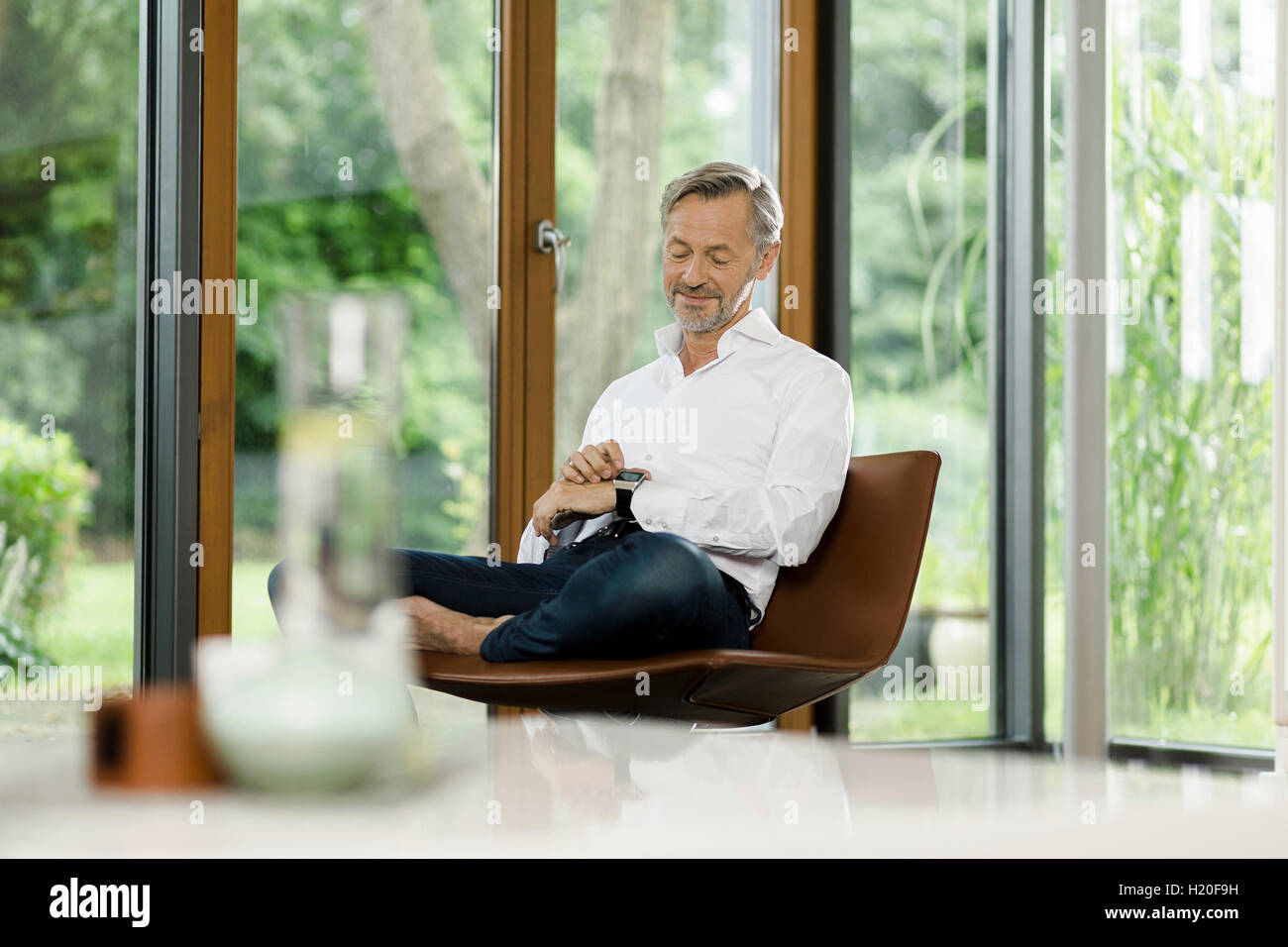 Man sitting on chair in his living room looking at smartwatch Stock ...