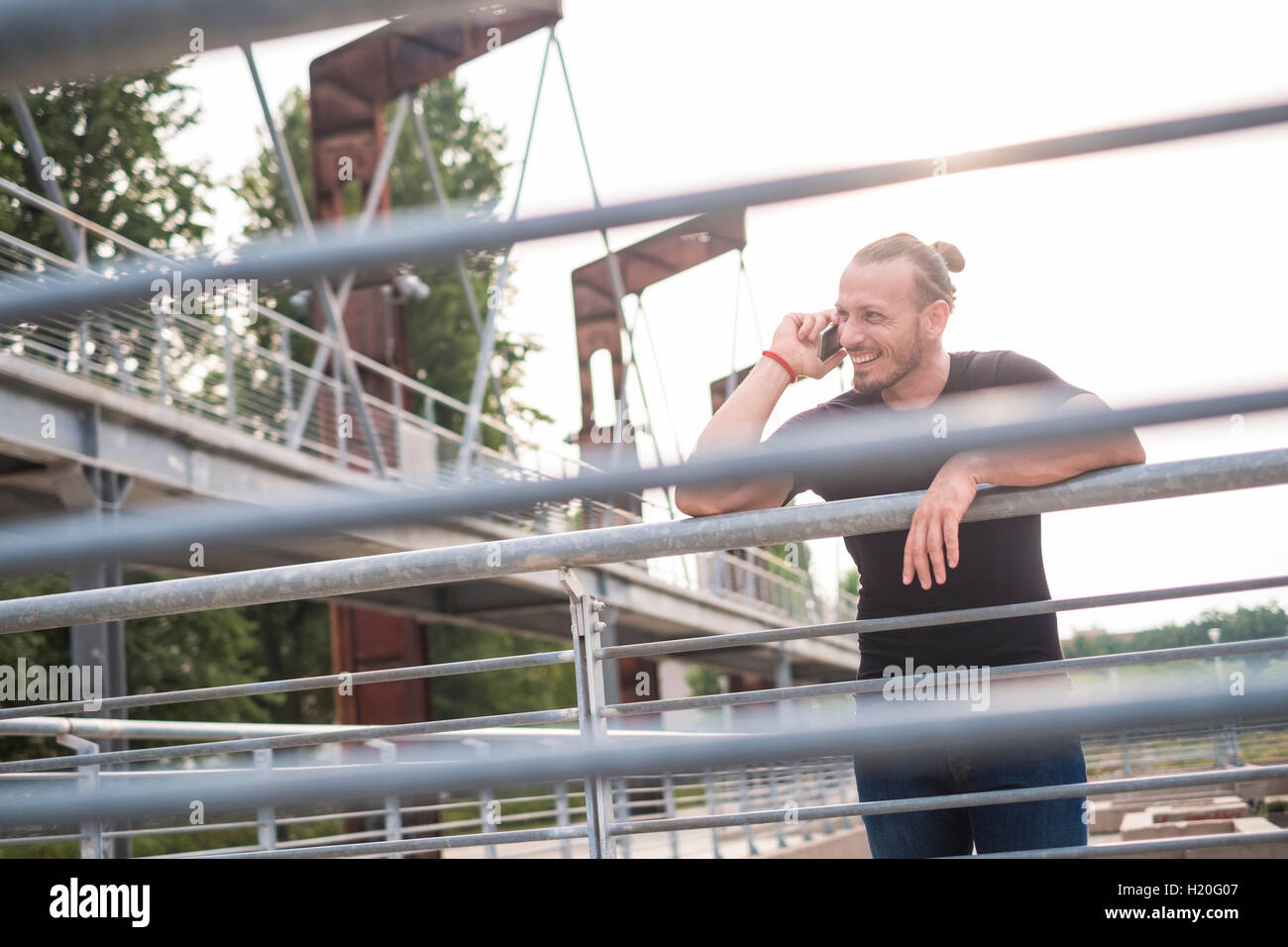 Smiling man on the phone leaning on railing Stock Photo - Alamy