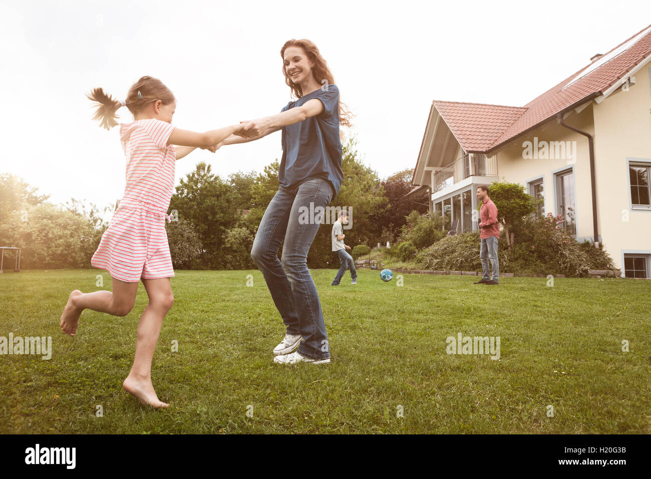 Mother and daughter dancing in garden with family in background Stock ...
