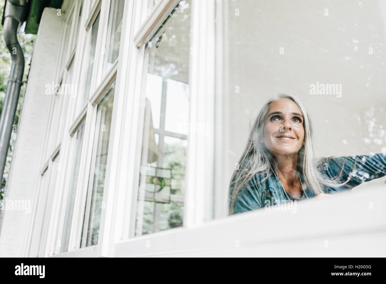 Smiling woman at home looking through window Stock Photo - Alamy