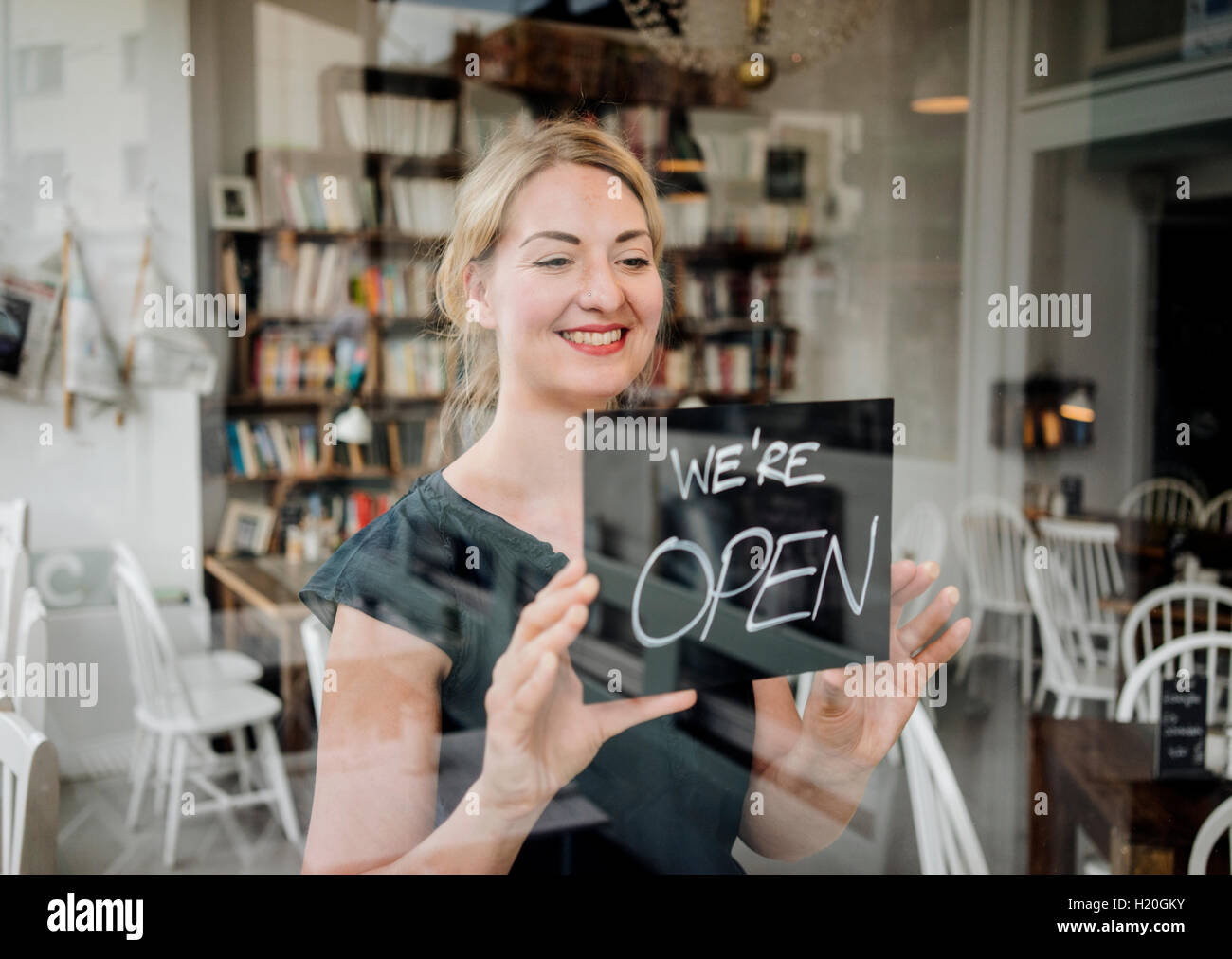 Smiling woman in a cafe attaching open sign to glass pane Stock Photo ...