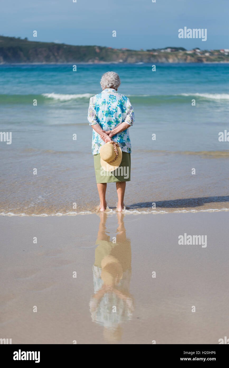 Back view of senior woman standing on the beach at seashore Stock Photo ...