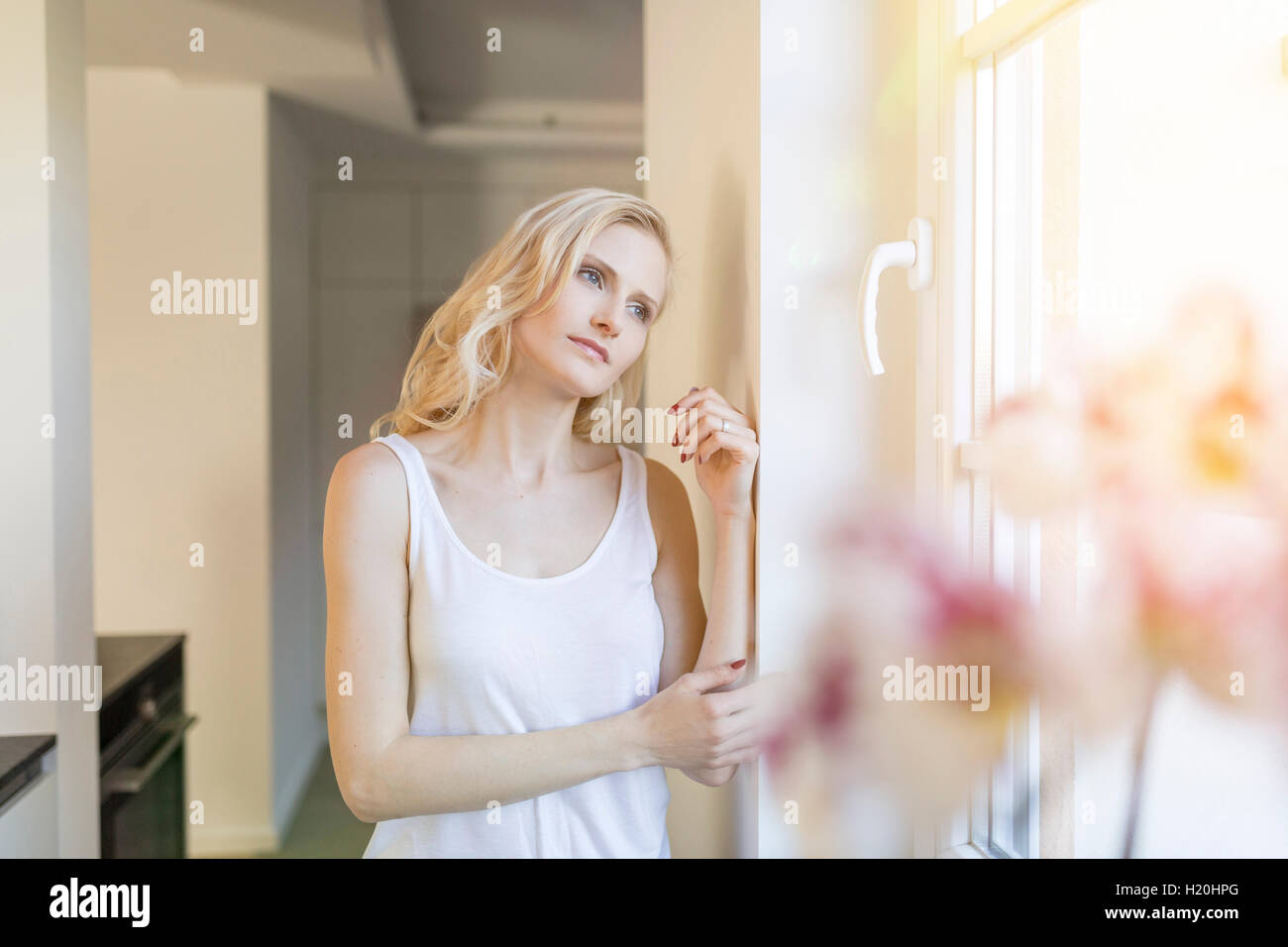 Blond woman at home looking out of window Stock Photo - Alamy