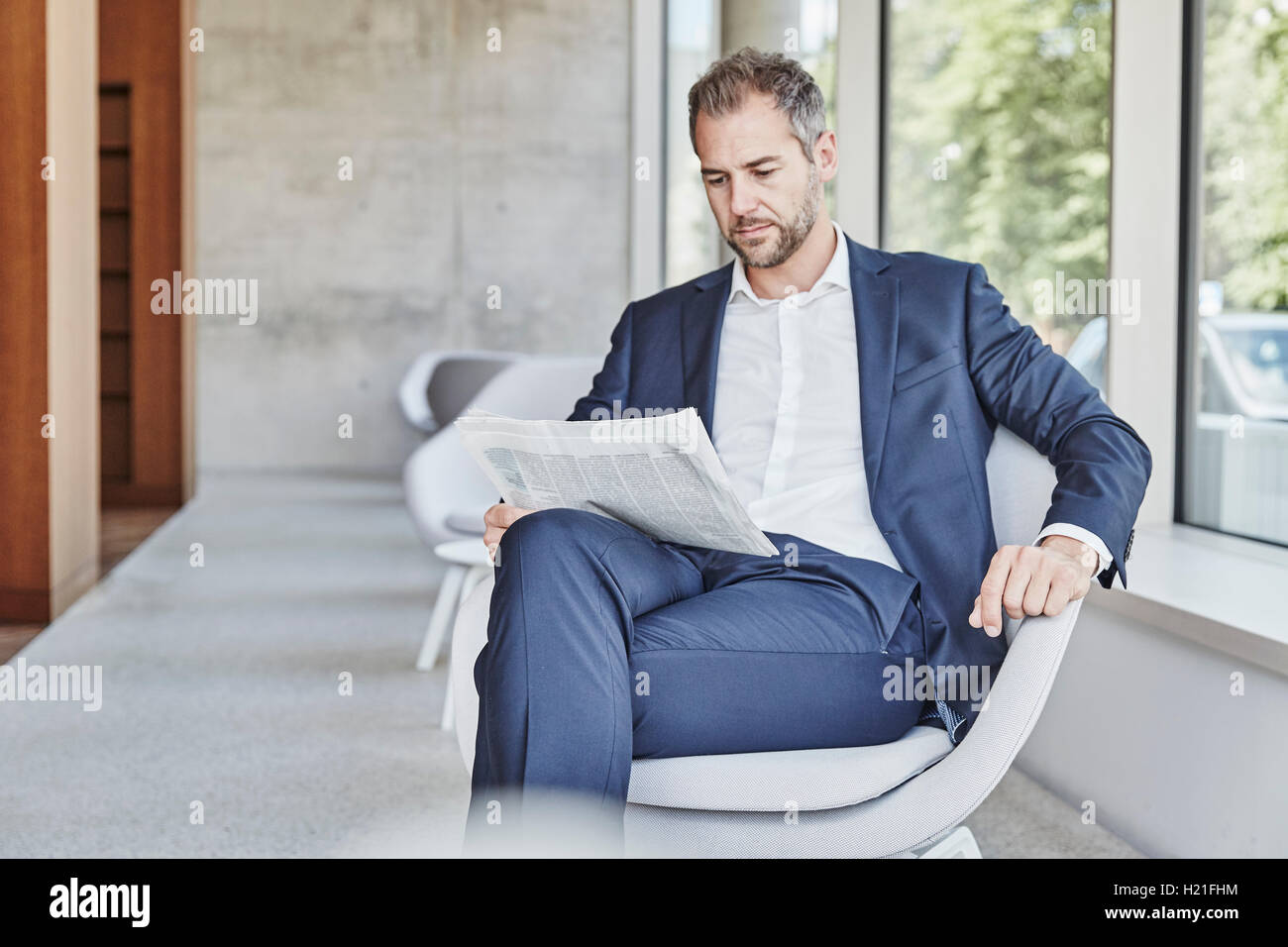 Businesssman sitting on chair reading newspaper Stock Photo - Alamy