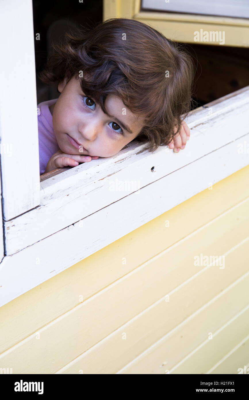 Portrait of little girl looking through open window Stock Photo - Alamy