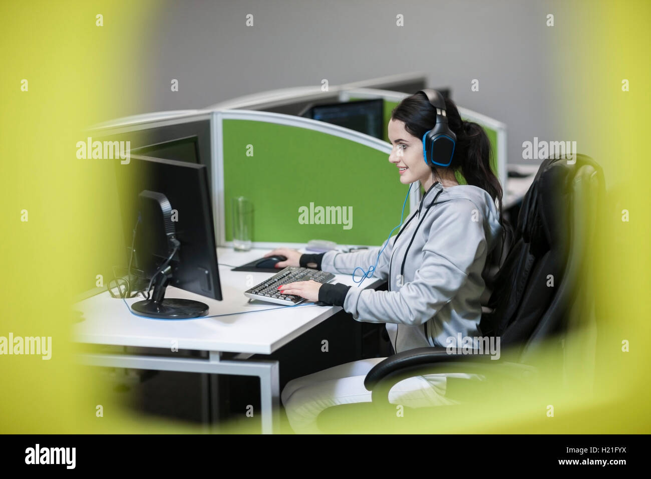 Young woman wearing headphones working on computer in office cubicle ...