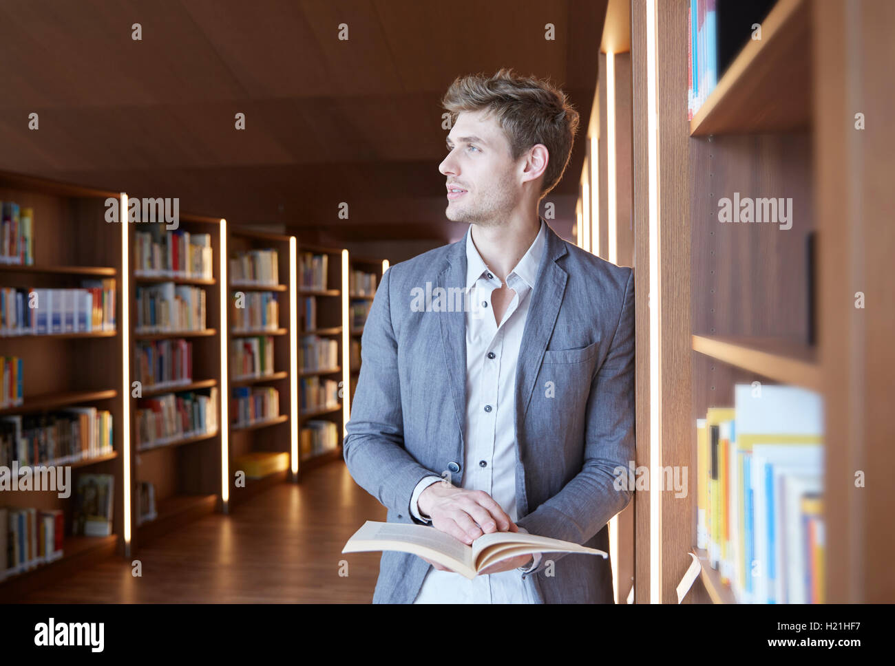 Young man with book in library Stock Photo - Alamy