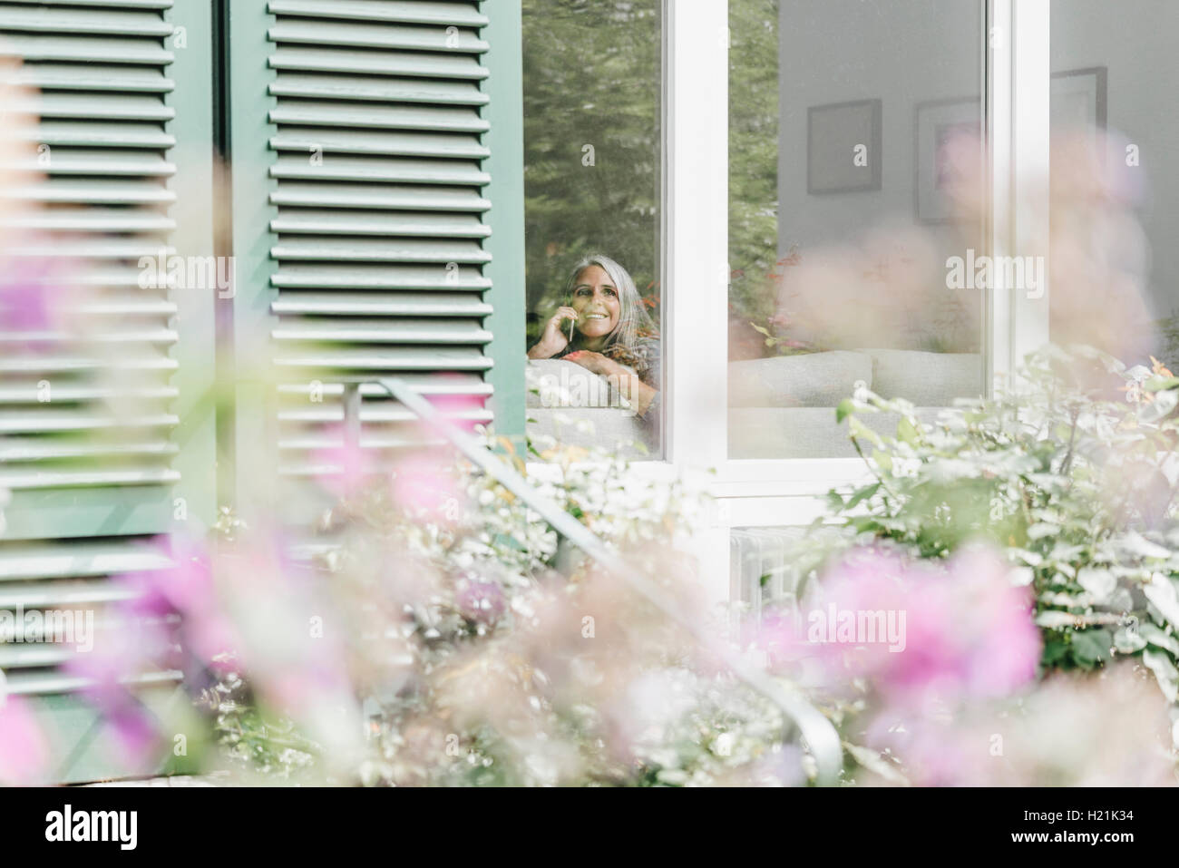 Woman on the phone sitting on the couch looking through window Stock ...