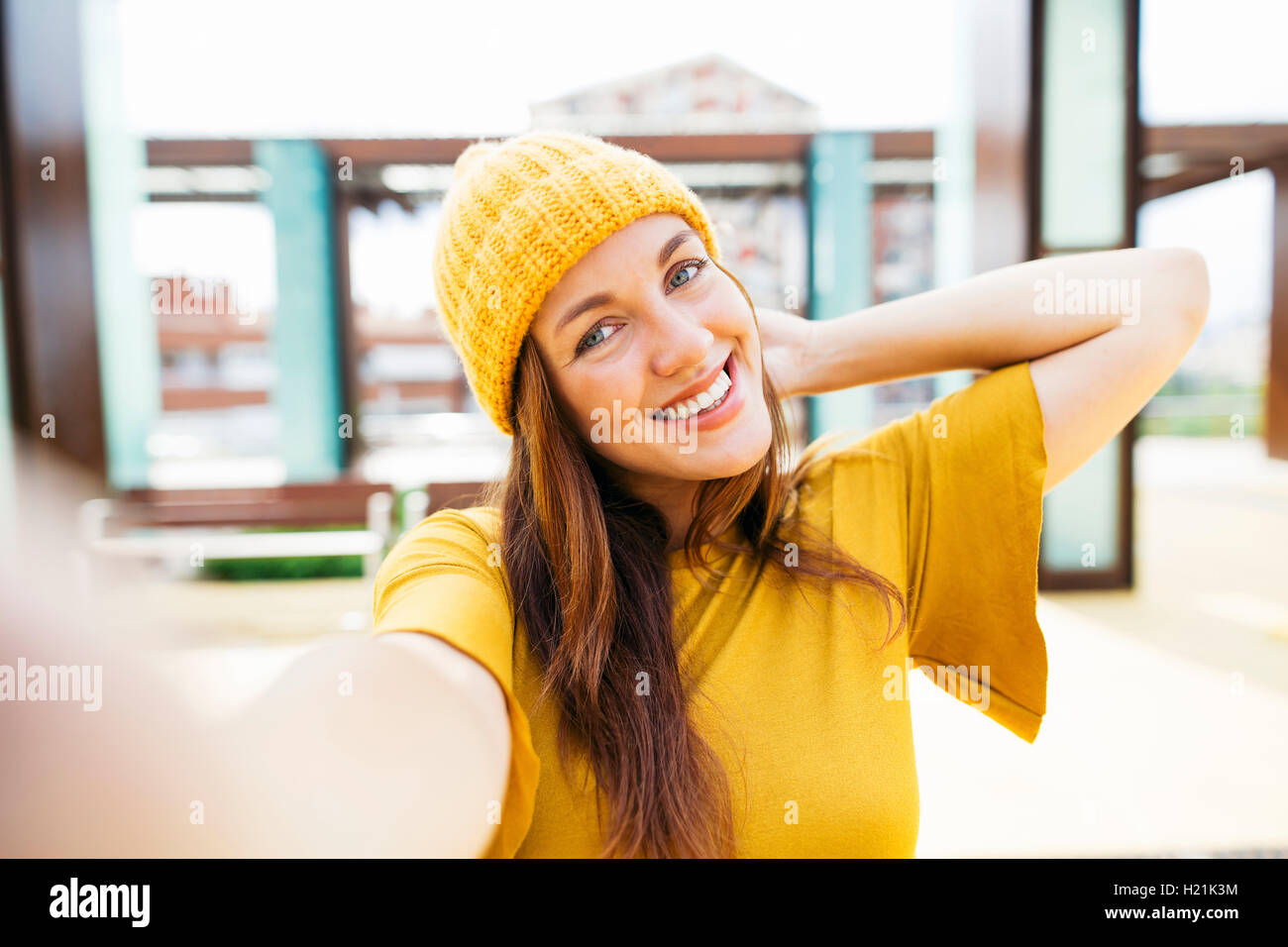 Portrait of smiling young woman wearing yellow clothes taking selfie ...