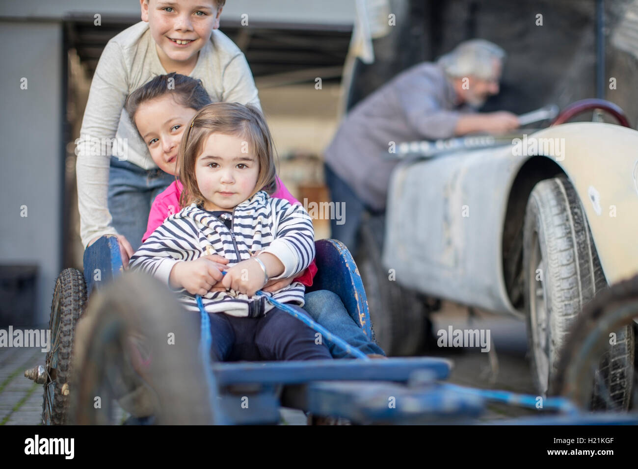 Boy pushing two little girls in go-kart Stock Photo - Alamy