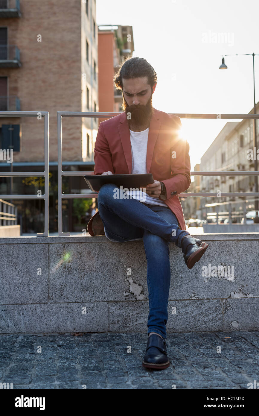 Young man sitting on a wall in the city using tablet Stock Photo - Alamy
