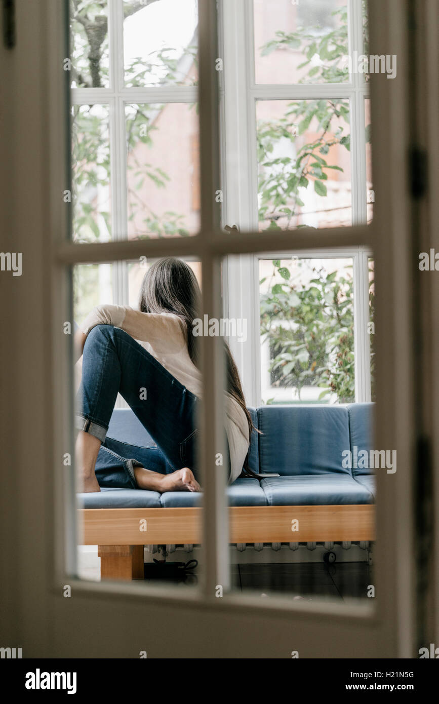 Back view of woman sitting on lounge in winter garden looking through ...