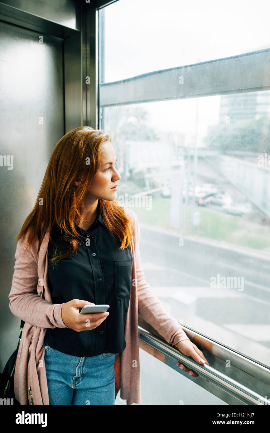 Serious young woman looking through window Stock Photo - Alamy