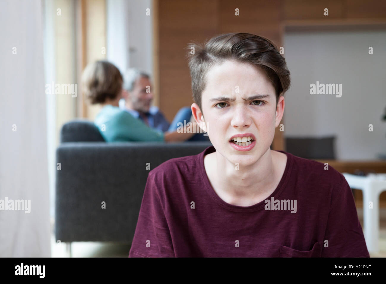 Portrait of angry teenage boy at home with parents in background Stock ...