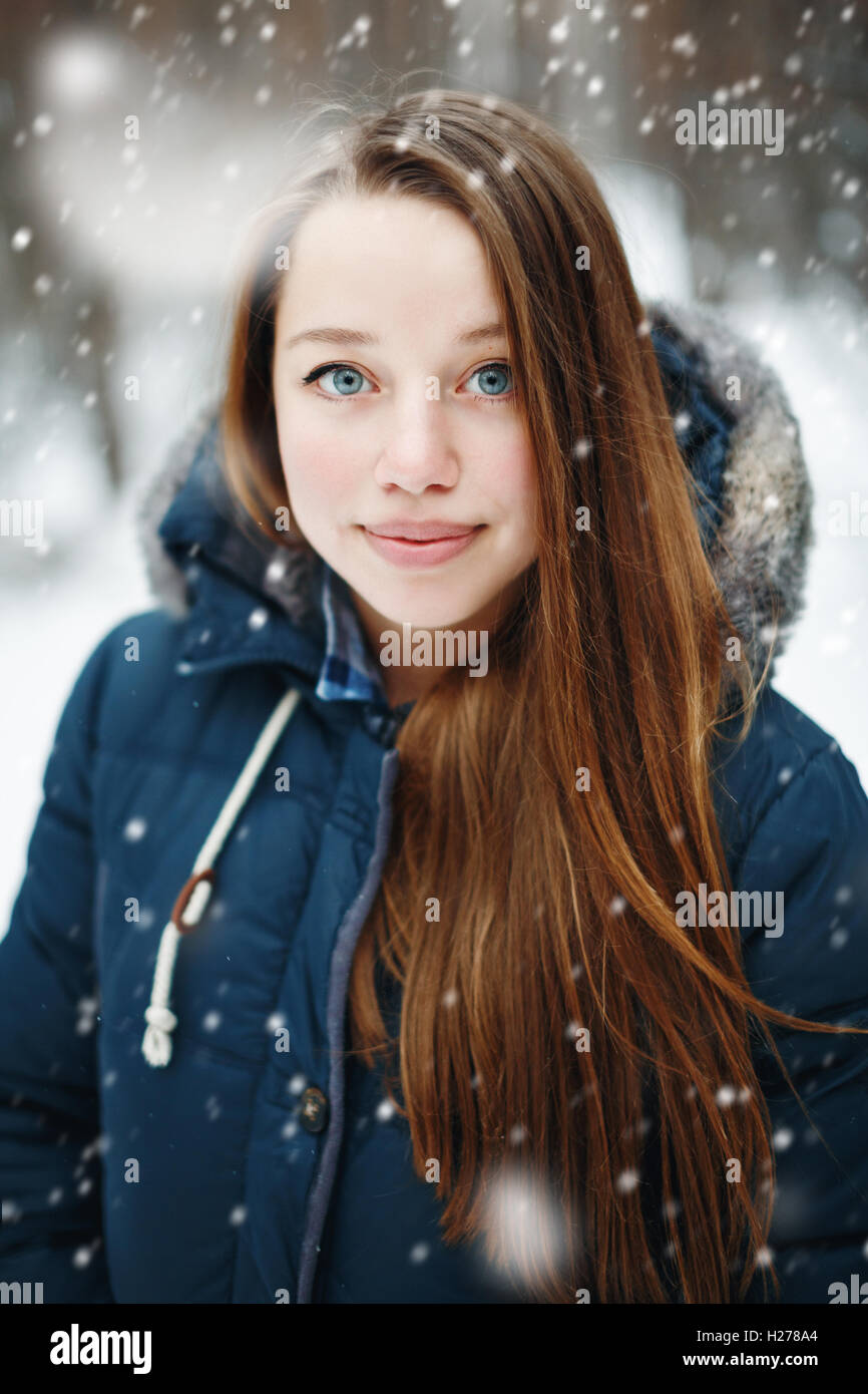 Young woman in winter clothes standing under the snow, smiling, looking ...