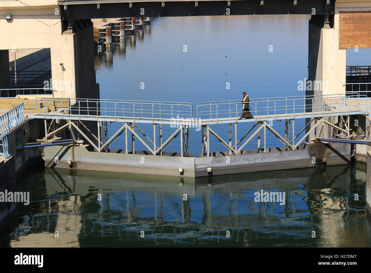 Man walks across small bridge at the Ship locks in Esna, and old dam on ...