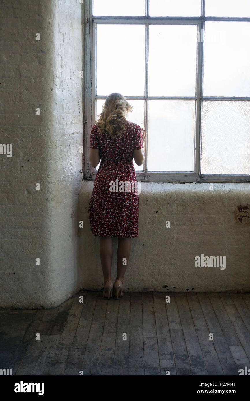 Rear view of a woman wearing vintage red dress standing by the window ...