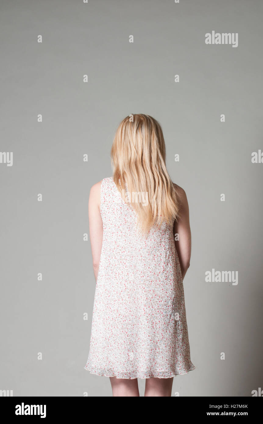 Rear view of a blond woman wearing a summer dress standing indoors ...