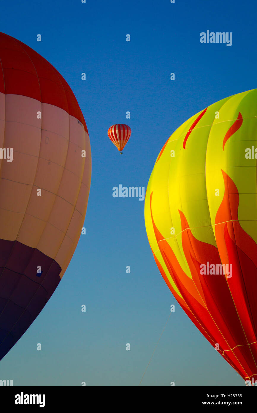 Vertical photo of three hot air balloons drifting across a blue sky ...