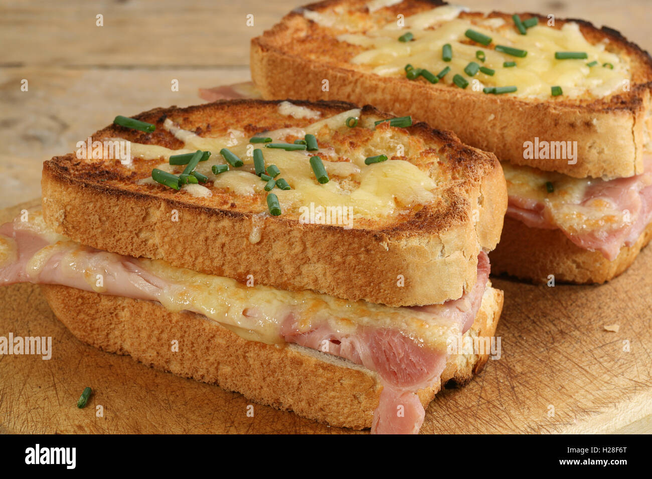 two slices of croque monsieur cheese and ham on a wooden board Stock ...