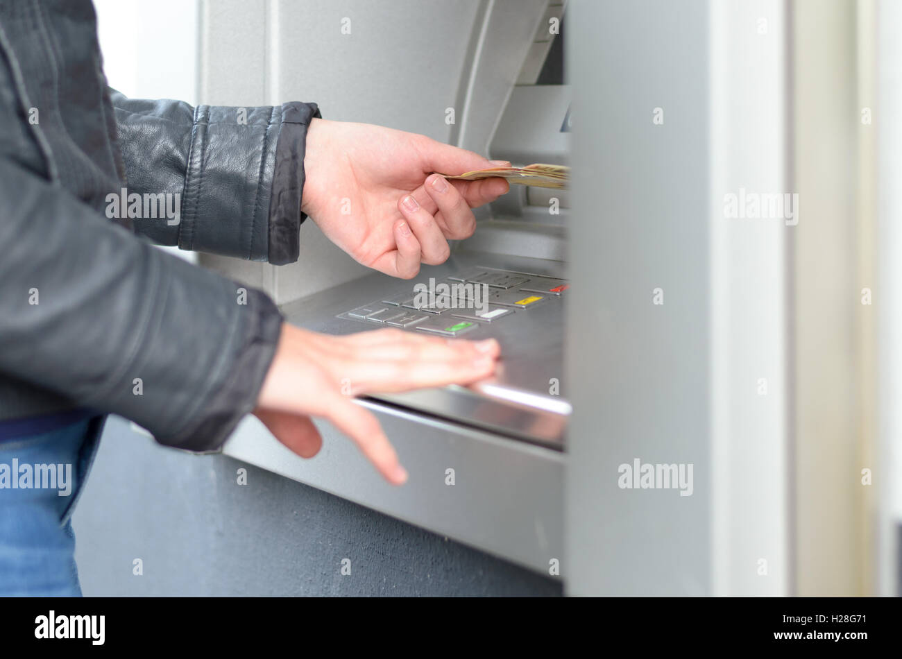 Young woman making a banking withdrawal at an outdoor ATM standing ...