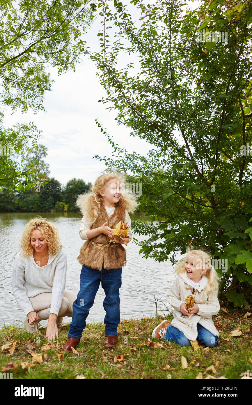 Two kids and woman in autumn collecting leaves at park near a lake ...