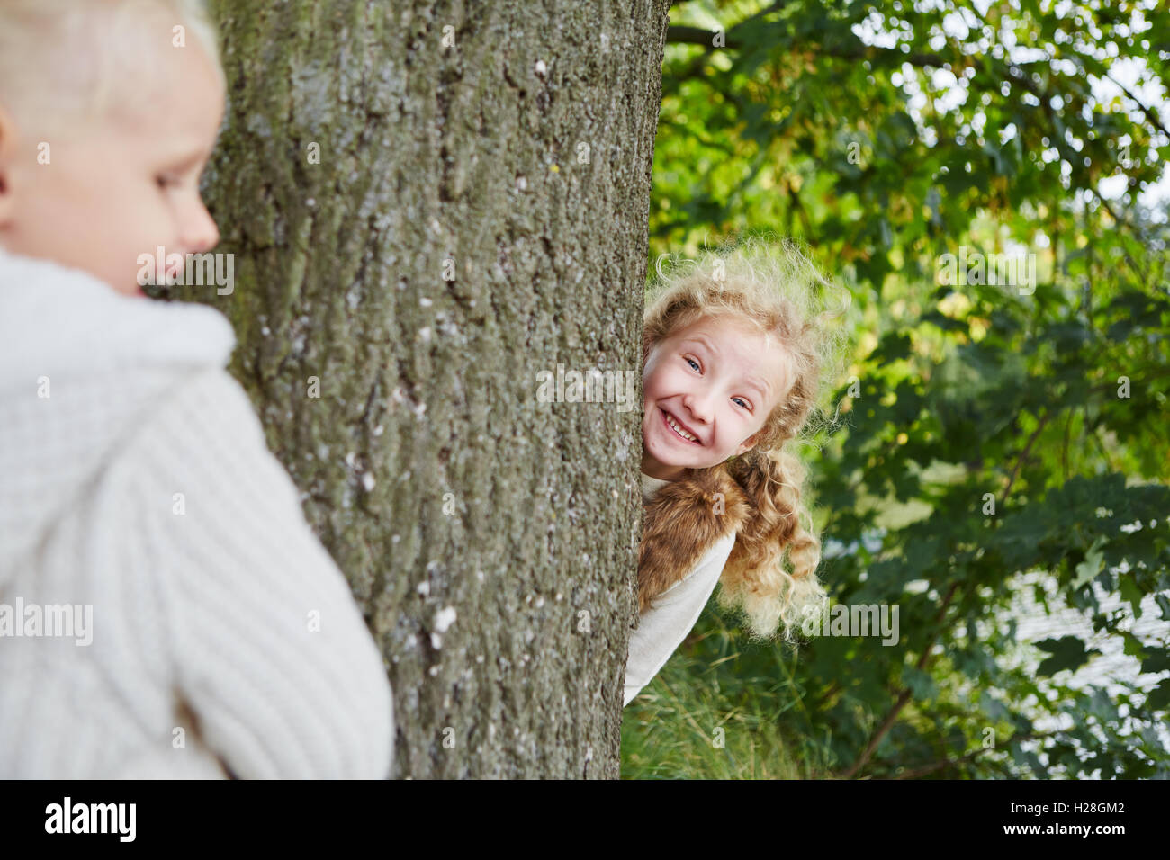 Two girls playing hide and seek in autumn at the park Stock Photo - Alamy