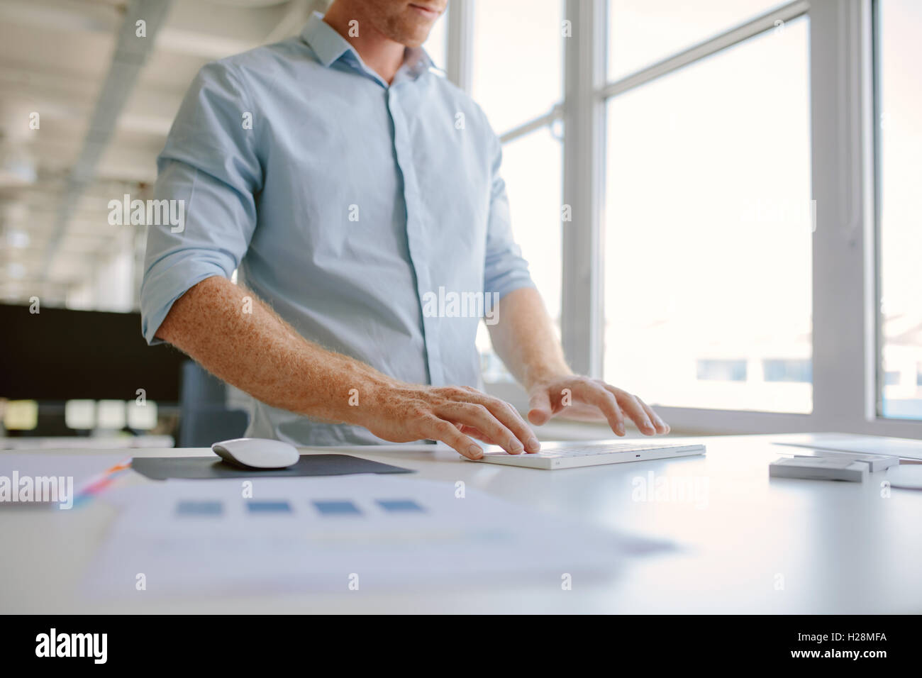 Cropped shot of young man standing at his desk and working on computer ...