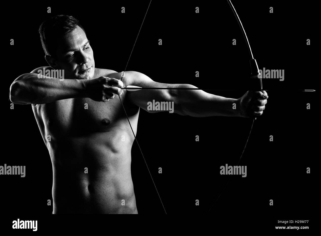 Shirtless guy aiming with a bow and arrow isolated on black background ...