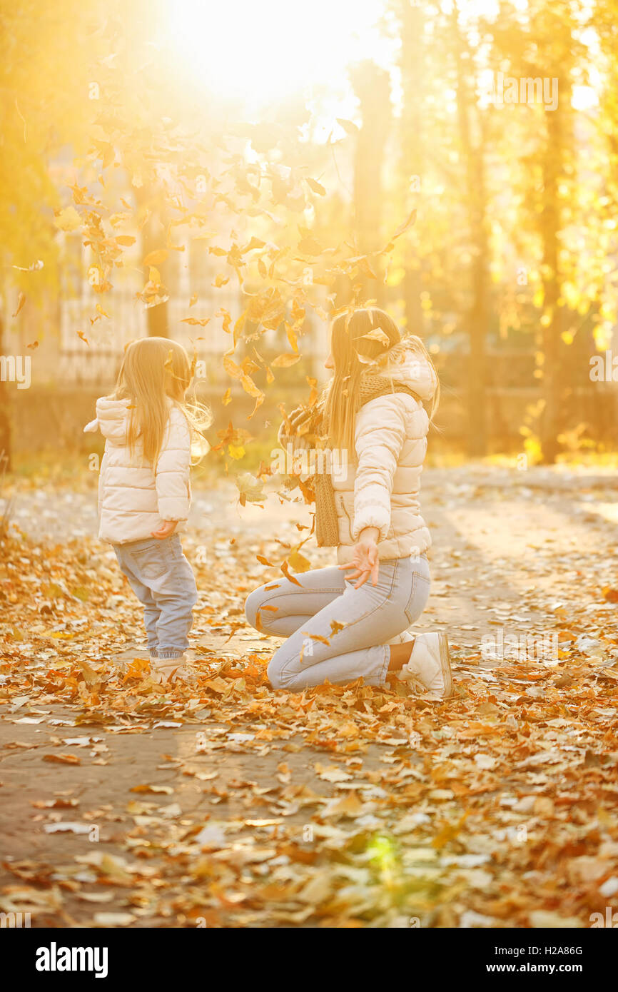 Family walk. Mother and daughter throw up fallen leaves. Autumn Park ...