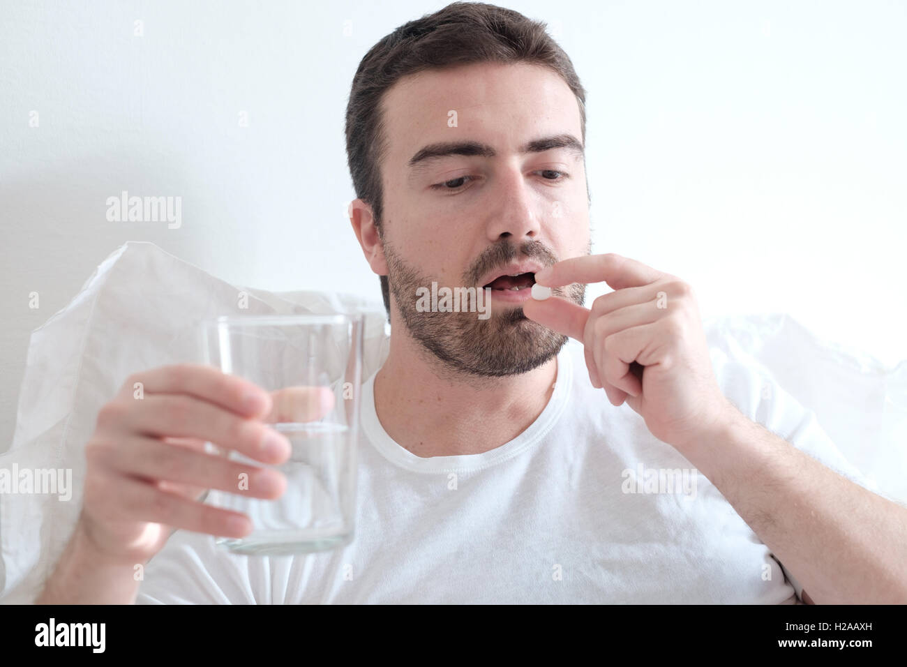 Man taking medicine pills lying in the bed Stock Photo - Alamy