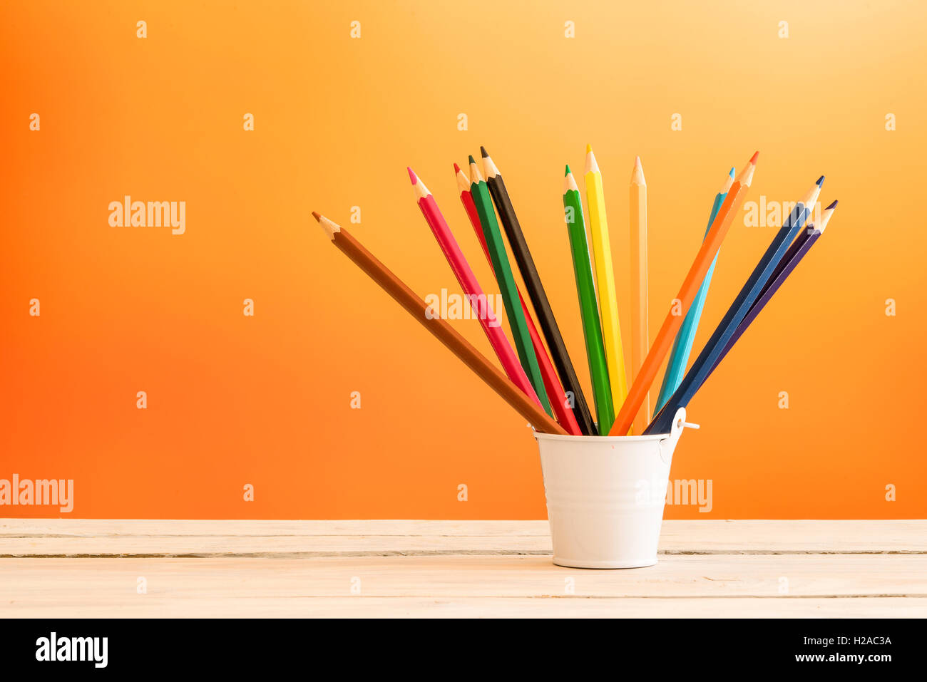 Color pencils in a white bucket on a wooden table Stock Photo - Alamy