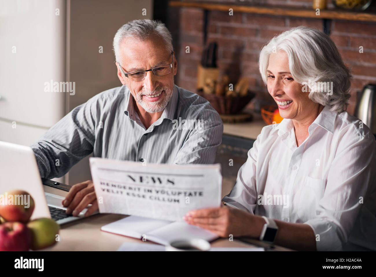 Likable old couple reading newspaper at the kitchen table Stock Photo ...
