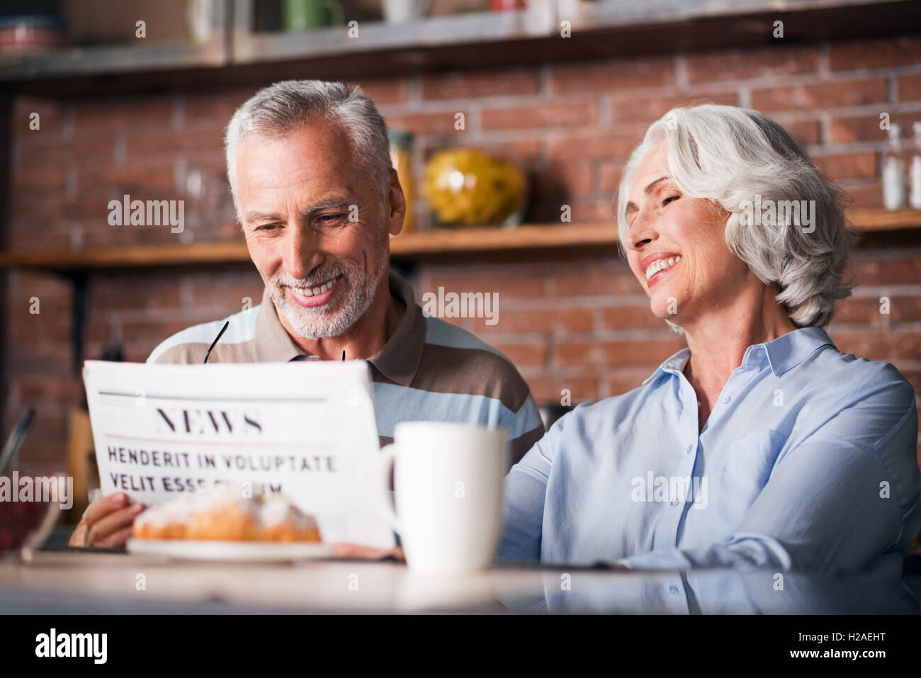 Grandparents reading newspaper together at kitchen table Stock Photo ...