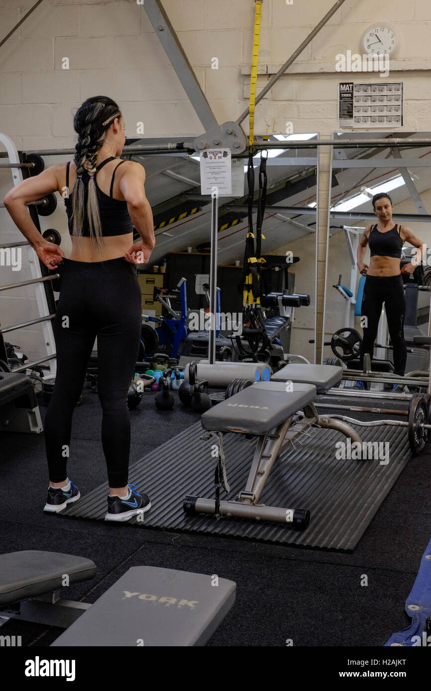 young female looking at herself in a mirror whilst working out in a gym ...