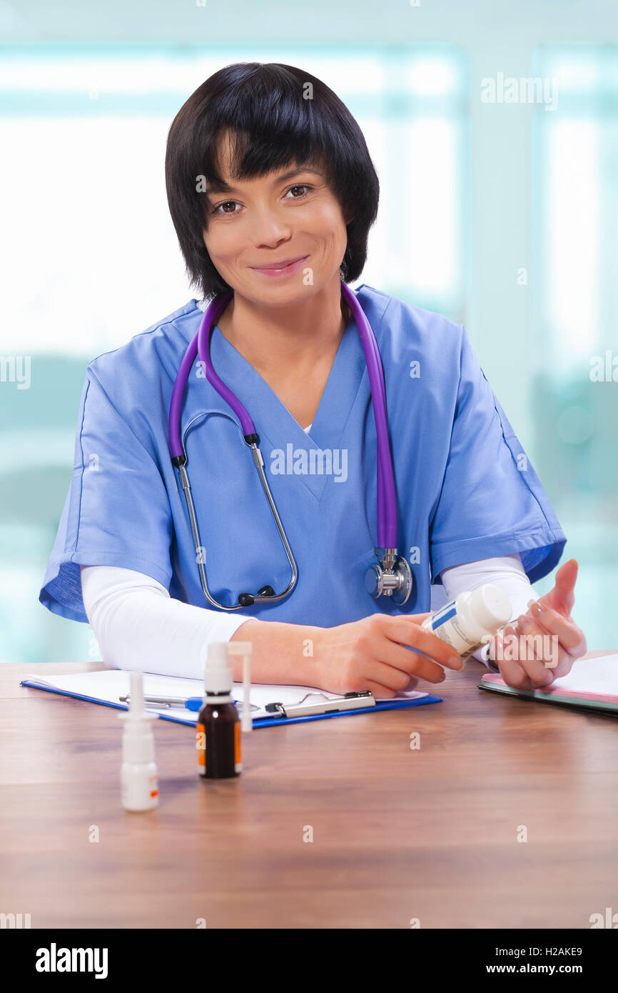 female doctor sitting at table and holding medical bottle Stock Photo ...