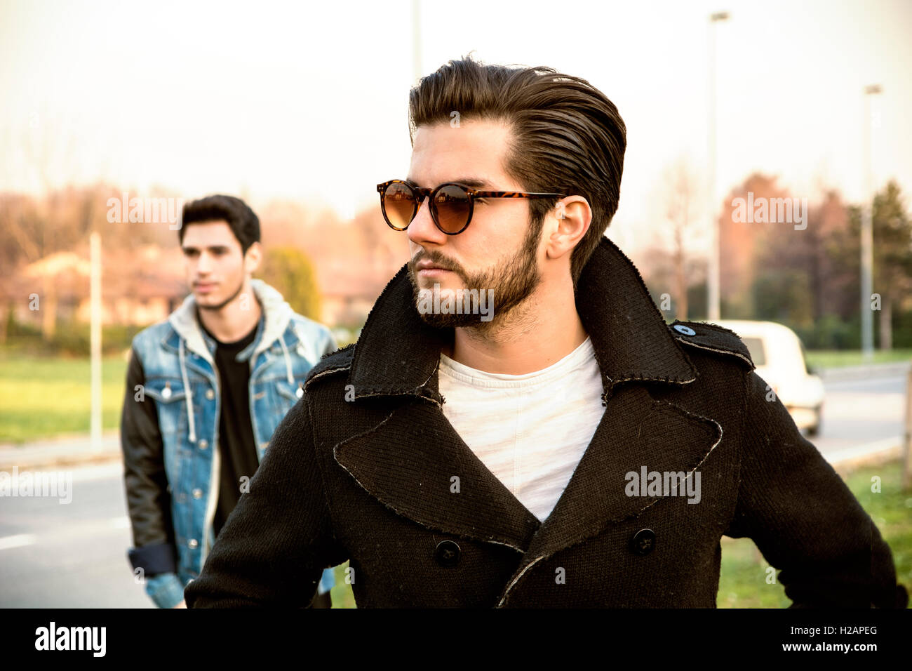 Two handsome casual trendy young men, 2 friends, in an urban park ...