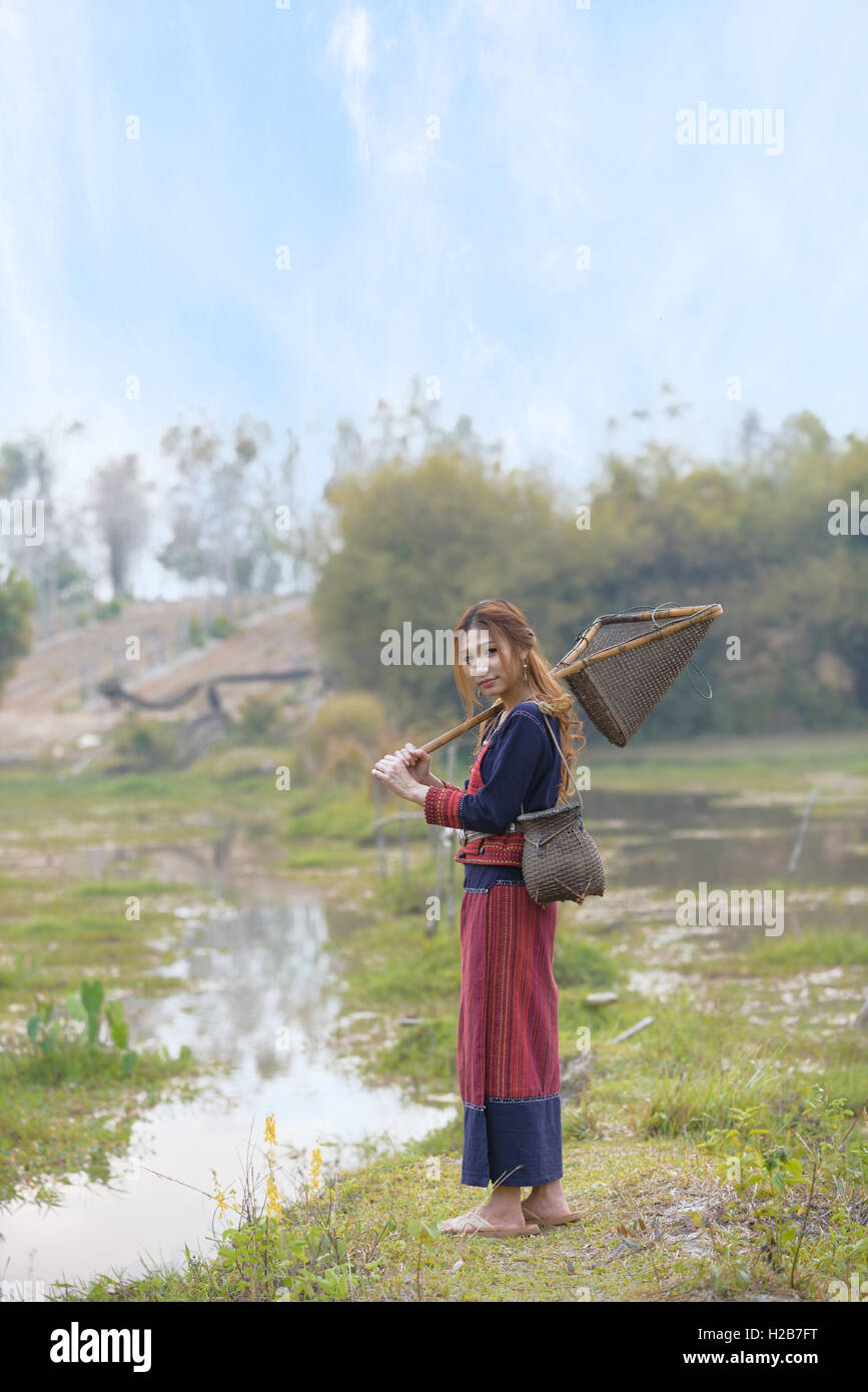 Asian beautiful lady in tribe dress stand near swamp with fishing gear ...