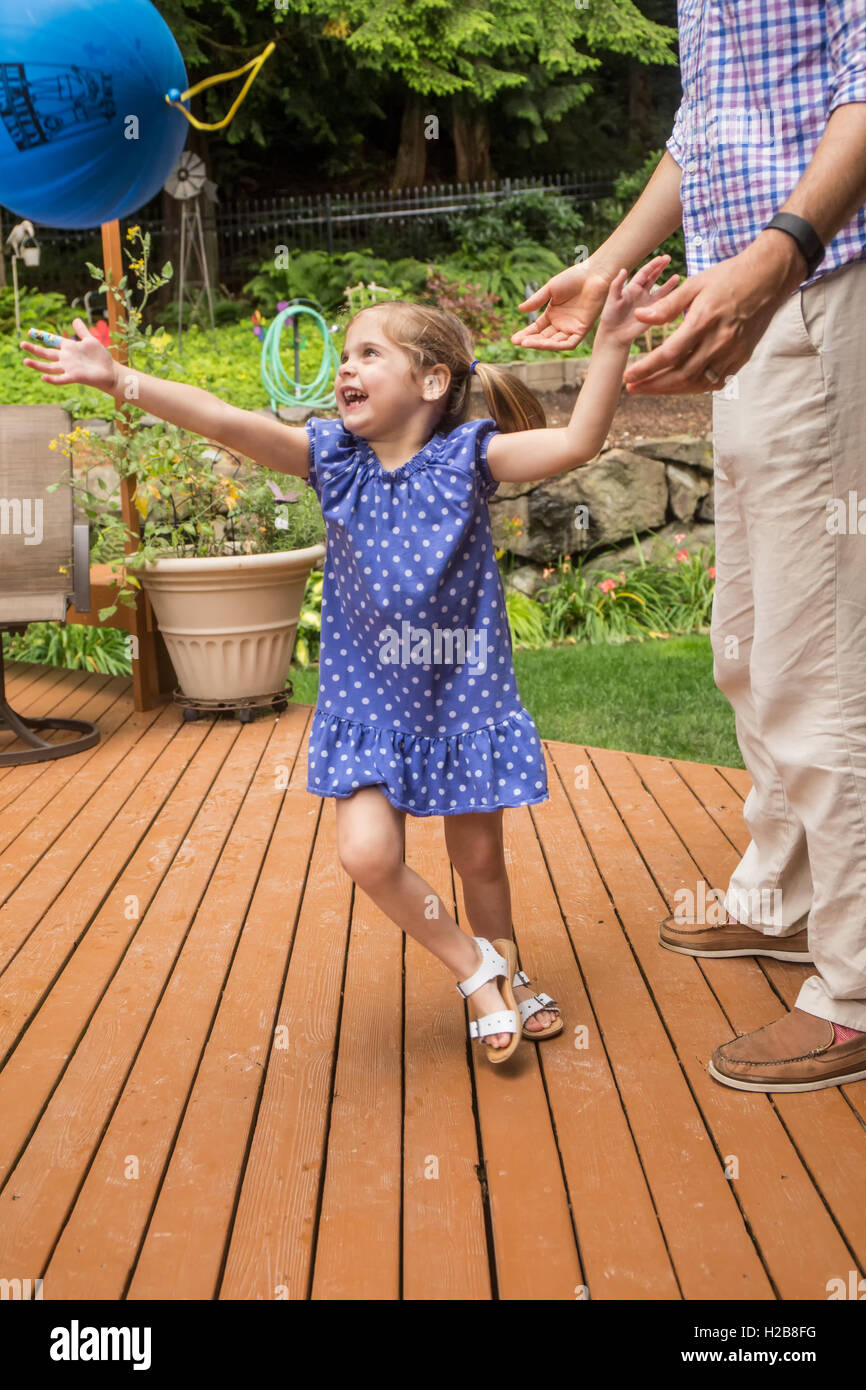Three year old girl trying to catch a balloon, with her father behind ...