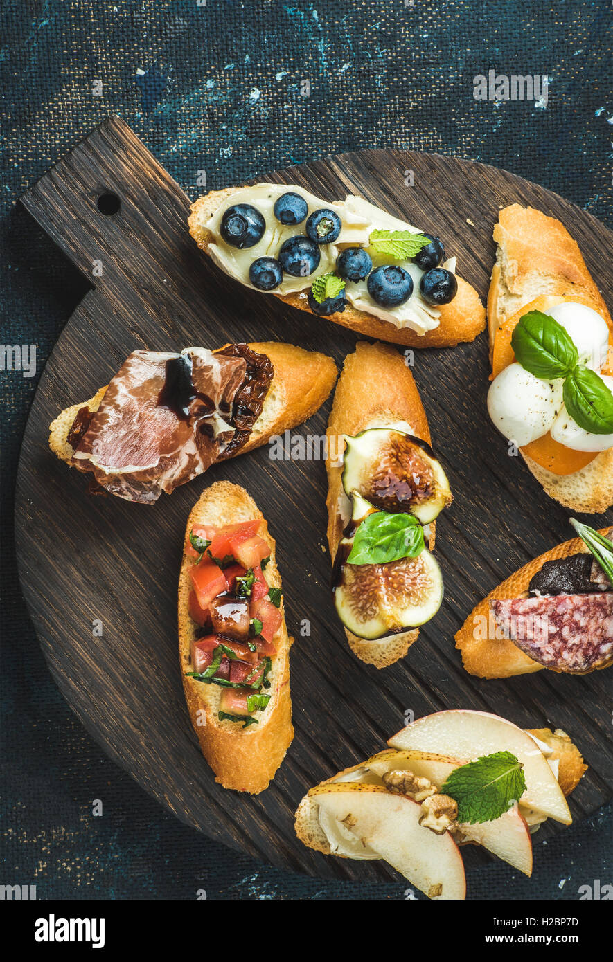 Italian crostini with various toppings on round wooden serving board ...