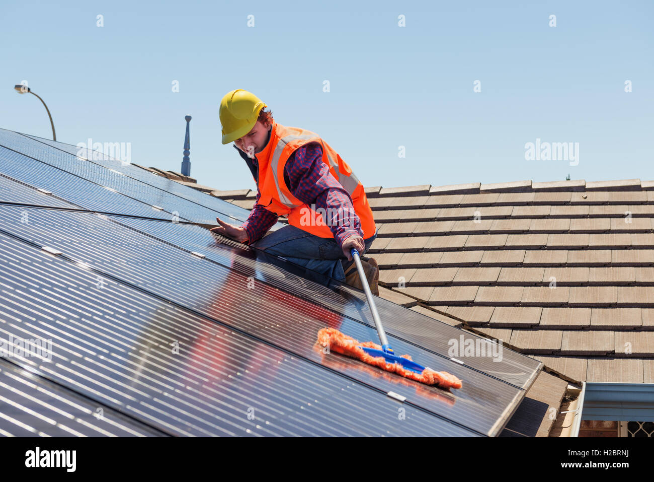 Young worker cleaning solar panels on the roof.Focus on the worker ...