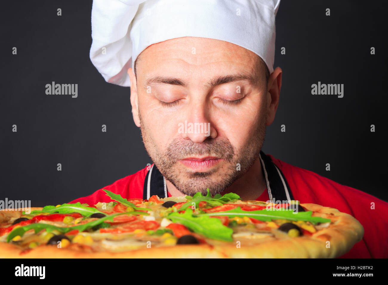 Portrait of happy attractive cook with a pizza in studio an a black ...
