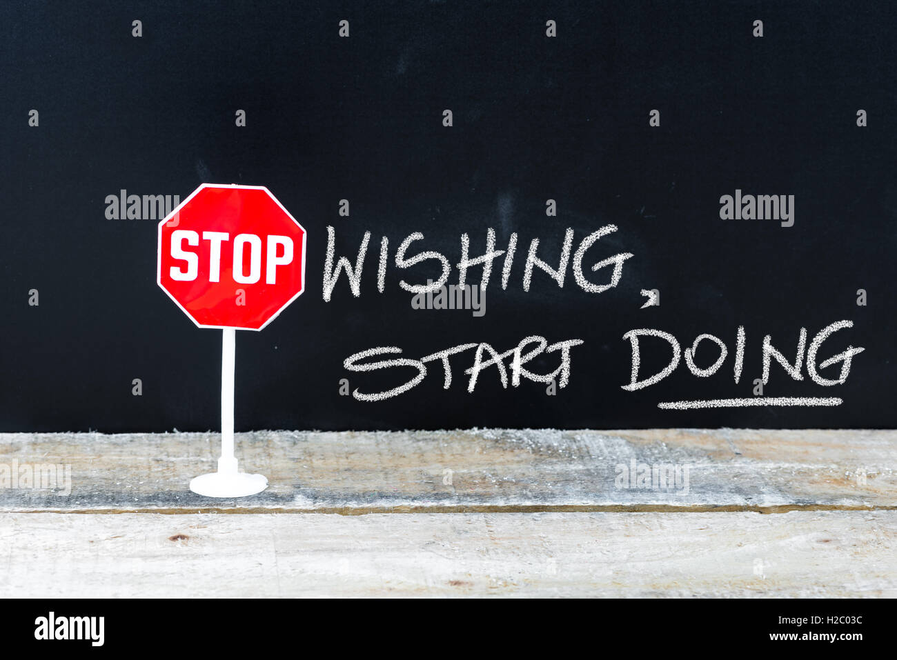 Mini STOP sign over chalkboard background and table, STOP WISHING START ...