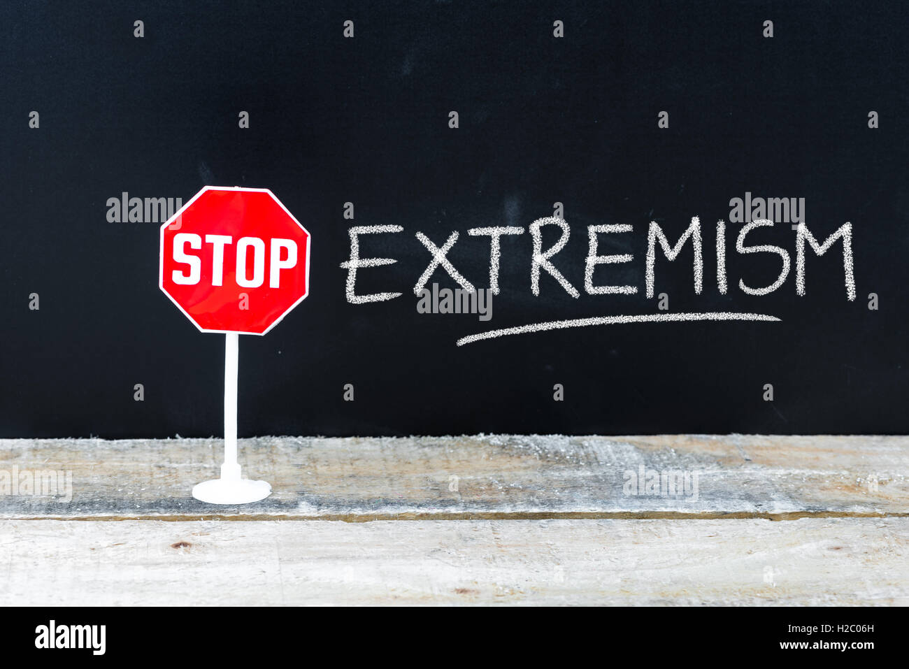 Mini STOP sign over chalkboard background and table, STOP EXTREMISM ...