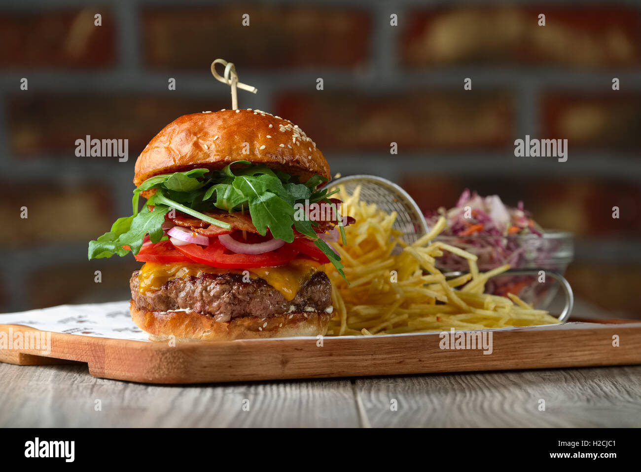 Burger on the wooden table with cheese, bacon, tomatos, green and red ...