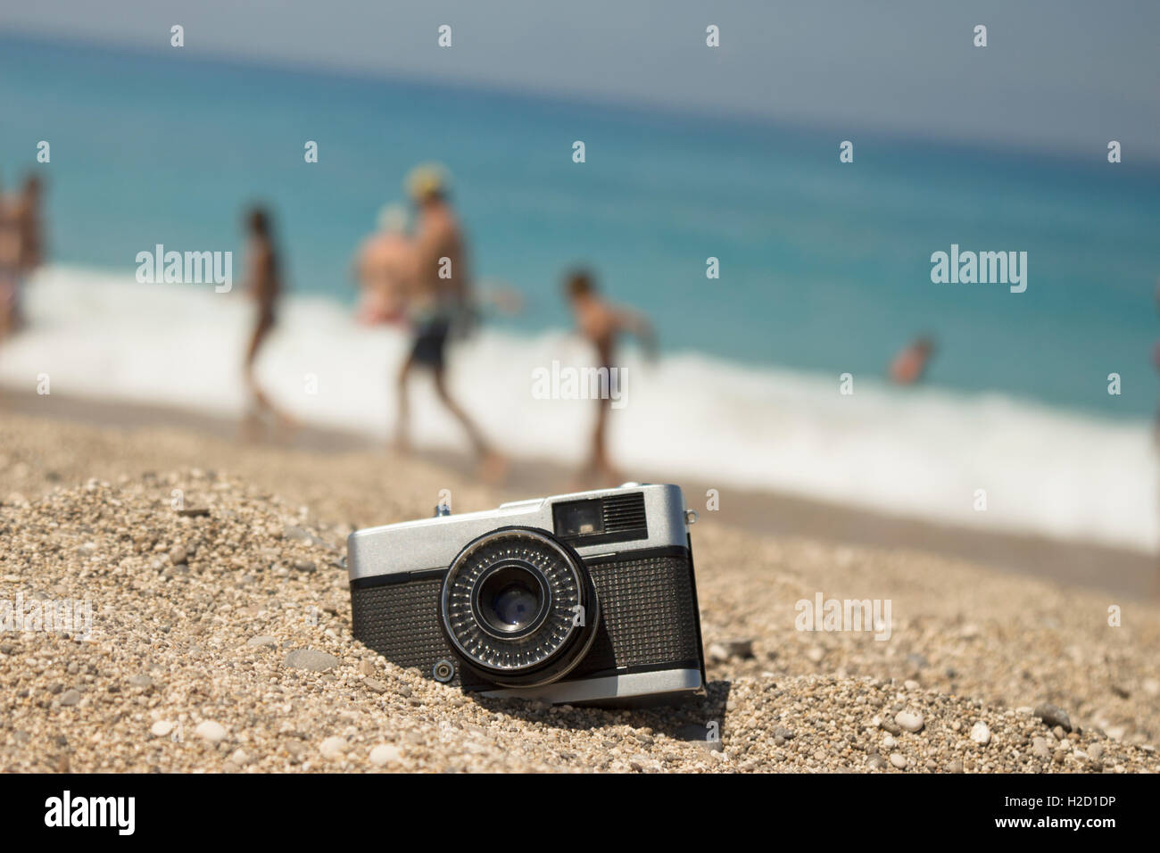 Vintage photo camera on pebble at the beach. Bathers in the background ...